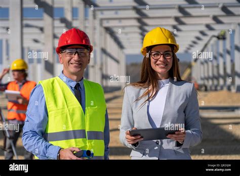 Smiling Man And Woman In Hardhats Looking At Camera Building And