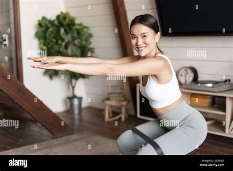 Cute Asian Fitness Girl At Home Doing Workout Squats With Stretching
