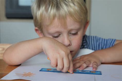 Little Boy Drawing And Using With Ruler Sitting At The Table Indoor