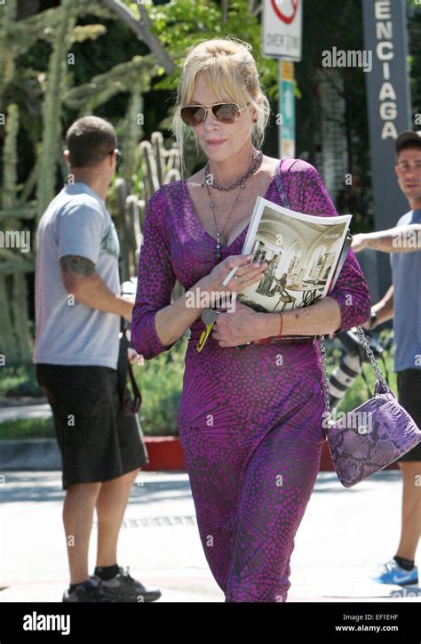 Melanie Griffith Wearing A Long Purple Patterned Dress And Smoking A Cigarette At Pacific Design