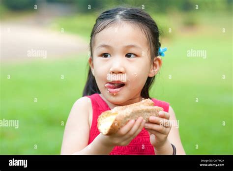 Little Asian Girl Eats A Sandwich And Licking Lips On Fresh Air Stock