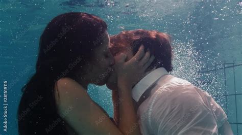 Romantic Couple Kissing Underwater In Swimming Pool Wearing Clothes