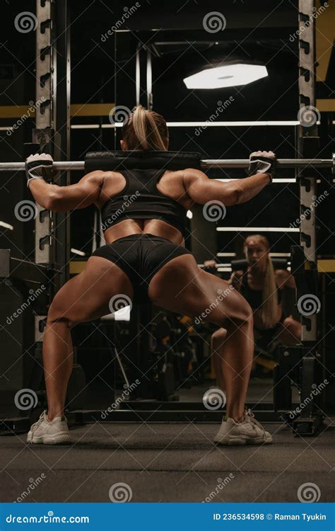 A Photo From Behind Of A Fit Woman Who Is Squatting With A Barbell In