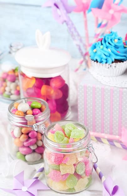 Premium Photo Multicolor Candies In Glass Jars And Cupcakes On Color Wooden Background