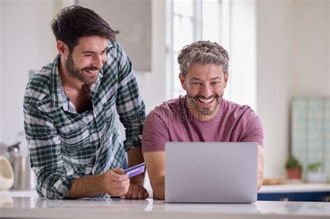 Same Sex Male Couple With Credit Card Using Laptop At Home To Book Same Sex Male Couple With Credit Card Using Laptop At Home To Book
