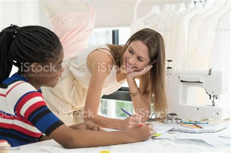 중소기업 개념입니다 양복점에서 함께 일하는 두 명의 여성 패션 디자이너 여성 양장점들이 재봉 작업장에서 직물 패턴 스케치에 대해 토론한다 18 19세에 대한 스톡 사진 및