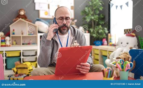 Young Bald Man Preschool Teacher Reading Document Speaking On The Phone