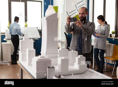 Architect Profession Man Looking At Maquette Layout Using Smartphone To Design Building Model