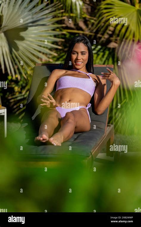A Young Latin Woman Is Lounging On A Sunbed In A Purple Bikini Smiling