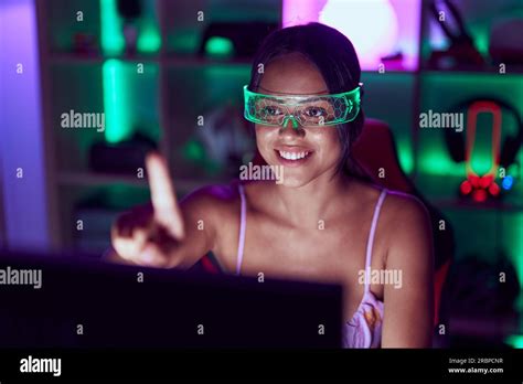 Young Hispanic Woman Streamer Using Computer And Virtual Reality Glasses At Gaming Room Stock