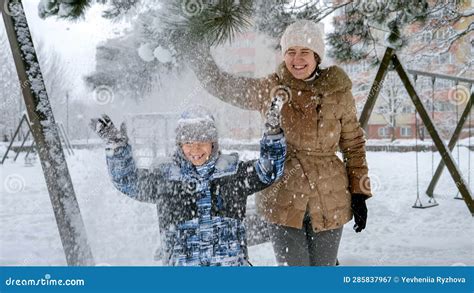Laughing Mother With Son Shaking Tree Branch And Enjoying Falling Snow