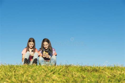 Two Teenage Girls Using Mobile In Park Stock Image Image Of