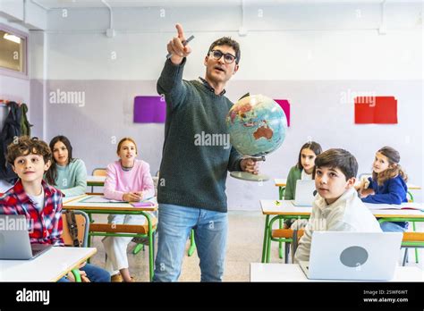 Geography Teacher Holding Globe And Pointing At Classroom Map While