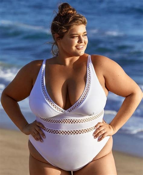 A Woman In A White Swimsuit Standing On The Beach With Her Hands On Her