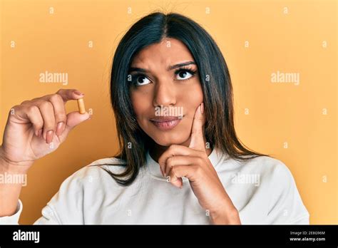 Young Latin Transsexual Transgender Woman Holding Pill Serious Face Thinking About Question With