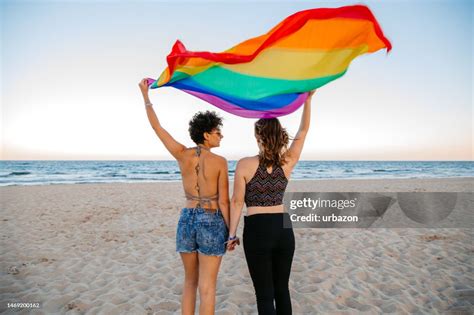 Young Lesbian Couple Holding Up An Lgbt Flag On The Beach High Res