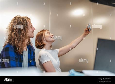 Side View Shot Of Couple Taking A Selfie At Work Short Haired Girl