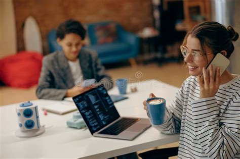 Female Programmer Is Talking Phone While Working On Laptop And Drinking