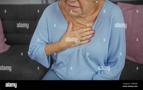 Elderly Woman Clutching Chest In Discomfort While Sitting On A Couch At
