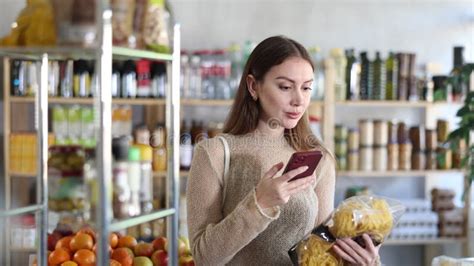 Female Buyer Checks Suitability Scans Qr Code On Pasta Label In A Grocery Store Stock Footage Female Buyer Checks Suitability Scans Qr Code On Pasta Label In A Grocery Store Stock Footage