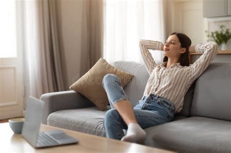 Relaxed Young Woman Lounging On Sofa In Front Of Laptop On Table Stock
