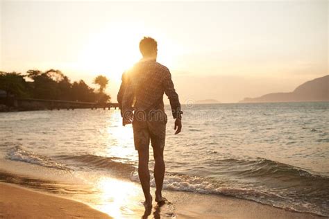 Man Walking On Beach And Ocean With Sunset Lens Flare With Back View