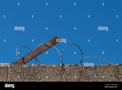 Concrete Wall Topped By Barbed Wire Seen Against A Blue Sky Stock