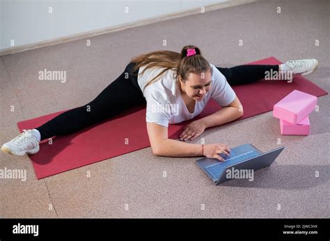 Young Caucasian Fat Woman Doing Bends On A Sports Mat And Watching A Training Video On A Laptop