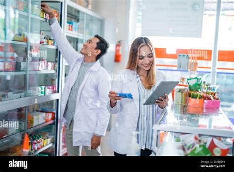 Asian Female Pharmacist In Uniform Using Pad To Check Medicine Stock