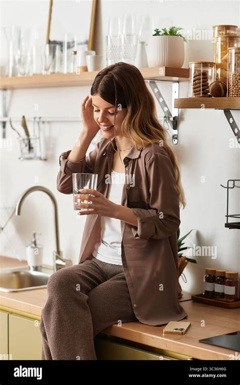 A Joyful Young Woman Sits On A Kitchen Counter Savoring Her Drink In