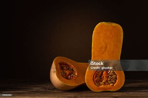 가을 채소 세로로 반으로 자른 잘 익은 호박이 짙은 갈색의 부드러운 배경에 밝은 반점이 있는 오래된 나무 탁자 위에 놓여 있습니다 버터넛 스쿼시 복사 공간이 있는 측면도
