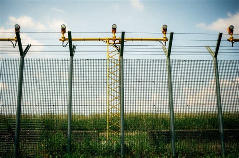 Airport Security Fence With Runway Approach Lights Behind A Green Wire