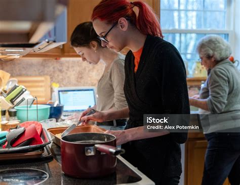 바쁜 부엌에서 가족 요리 그녀의 할머니와 여동생이 모두 백그라운드에서 요리하는 동안 십대 소녀는 파이팬을 기름칠 16 17 살에