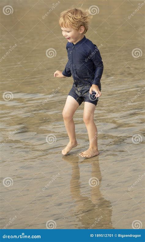Young Boy With Blonde Hair And Navy Swimsuit Having Fun Splashing At