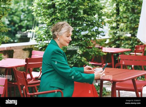 Outdoor Portrait Of Pretty Middle Age 55 60 Year Old Woman Relaxing In Cafe Using Phone Stock