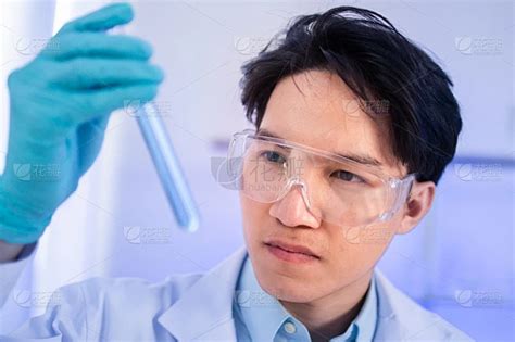 一名亚洲男性科学家正在科学实验室的科学试管中观察蓝色液体。素材 花瓣网