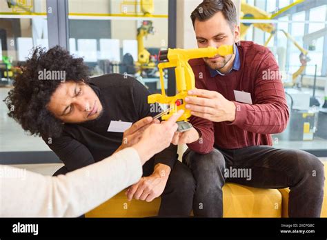 Two Engineers Closely Inspecting A Robotic Arm Model During A Technical Training Session Focused