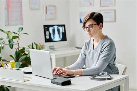 Premium Photo Young Serious Female Doctor In Medical Scrubs Typing On