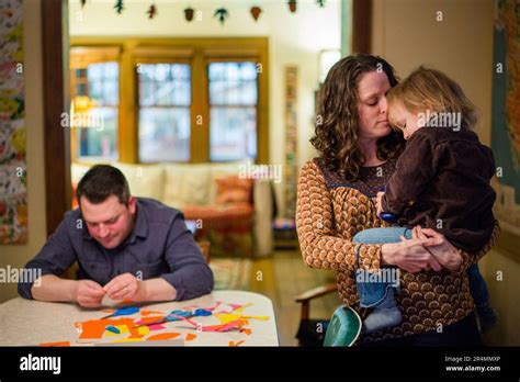 A Mother Tenderly Holds Her Preschool Son While Dad Sits In Background