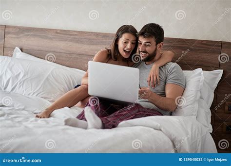 Happy Couple Lying On A Bed With Computer Beautiful Married Couple Watching Sex Video On