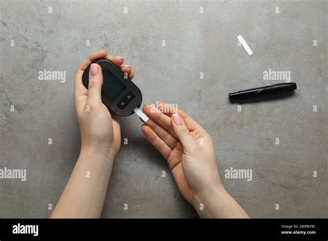 Diabetes Woman Checking Blood Sugar Level With Glucometer At Gray