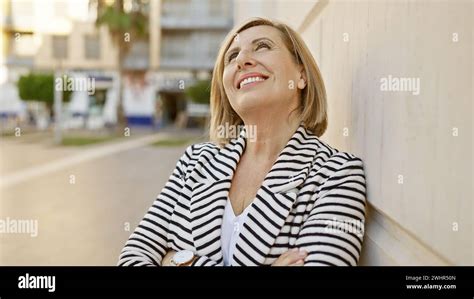 Mature Caucasian Woman Standing Outdoors In A City Smiling While Leaning Against A Wall Dressed