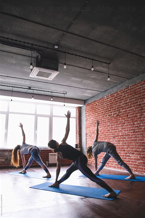 Three People Standing In Revolved Triangle Pose By Stocksy