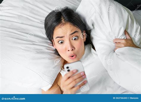 Portrait Of Asian Girl Wakes Up In Morning Looks At Mobile Phone With