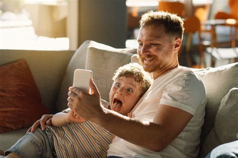 Father And Son Sit Relax On Couch In Hotel Hall Have Fun Using