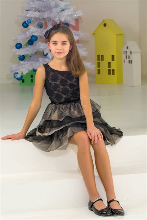 Girl In Stylish Dress Sitting On The Floor In Front Of Christmas Tree