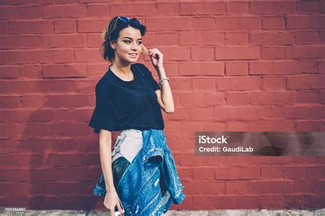 힙스터 라이프 스타일과 트렌디 한 스트리트 패션의 개념 행복한 평온한 여성 십대는 벽 근처의 홍보 영역에서 머리와 기다리는 친구와 함께 놀고 있는 동안 멀리 보이는 캐주얼