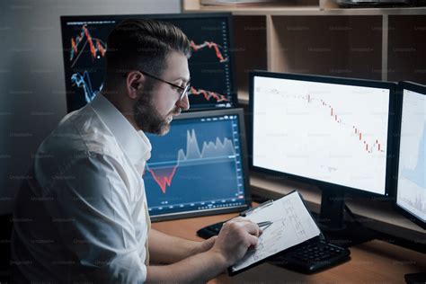 메모장 사용 흰 셔츠를 입은 수염 난 남자는 인덱스 차트에 여러 컴퓨터 화면이 있는 사무실에서 일합니다 사진 Unsplash의 우크라이나 이미지