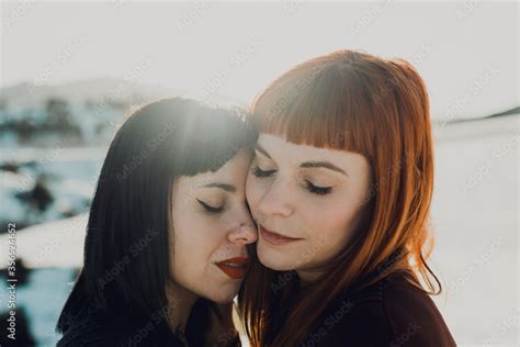 Side View Of Modern Sensual Lesbian Couple In Love Embracing While Standing In Back Lit In Snowy