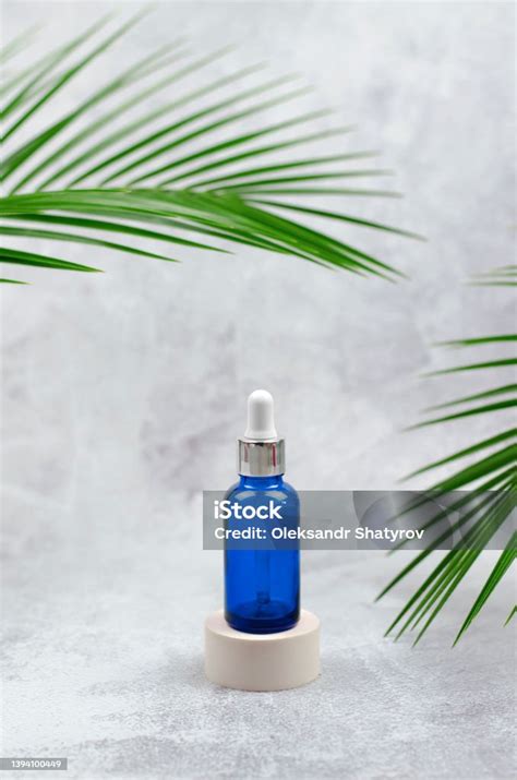 야자수 잎이있는 연한 회색 배경에 둥근 베이지 색 연단에 피펫이있는 파란색 화장품 병 얼굴과 몸을위한 천연 케어 화장품 0명에 대한 스톡 사진 및 기타 이미지 Istock